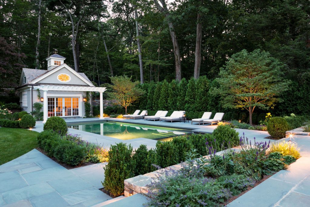 Shingle-Clad Pool House at the Edge of a Lush Backyard Oasis