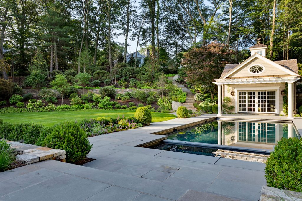 Shingle-Clad Pool House at the Edge of a Lush Backyard Oasis